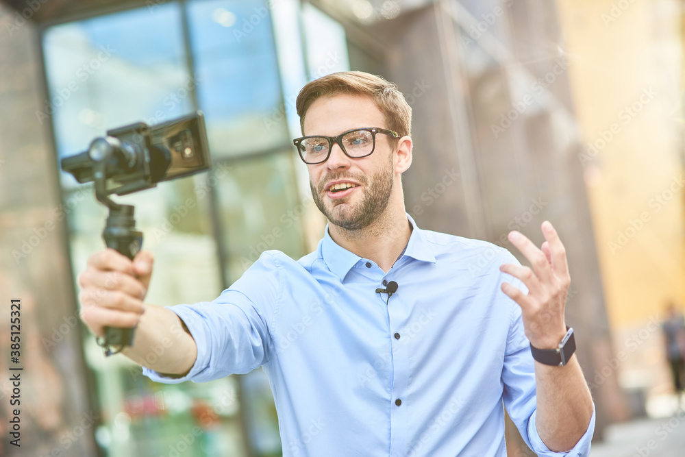 Young male vlogger wearing blue shirt and eyeglasses holding a gimbal ...