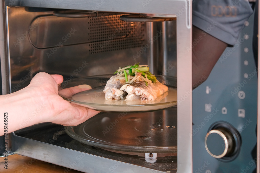 A housewife steaming fish in a microwave oven for a family dinner. She ...
