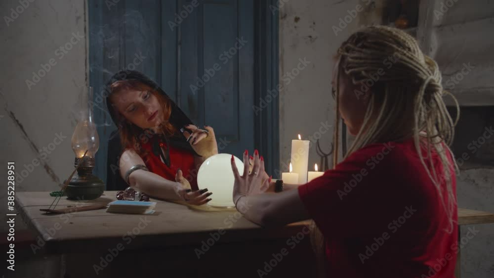 Lovely mystic fortune teller in black cape and woman holding hands ...