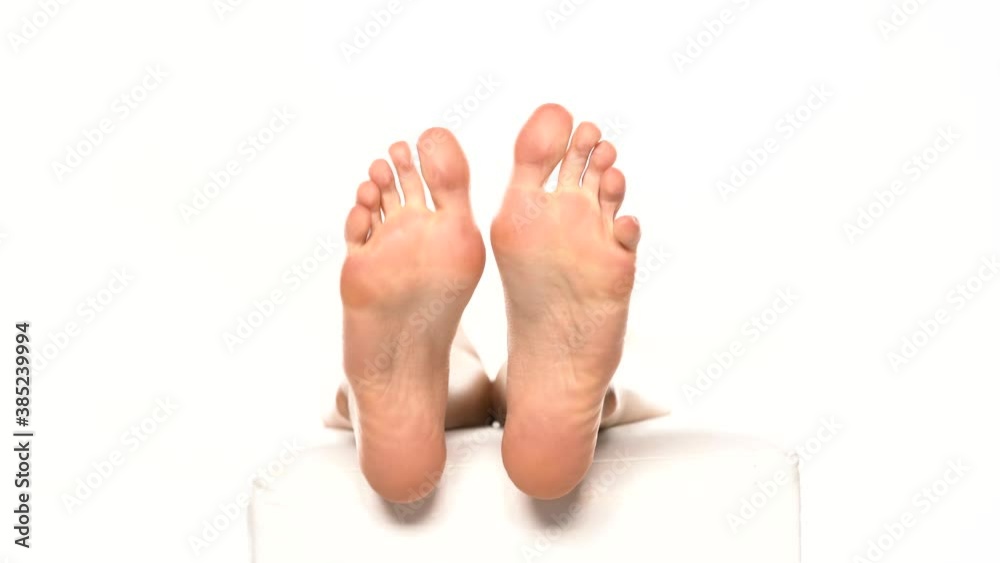 a woman lying on the bed and slowly moving her bare feet on a white ...