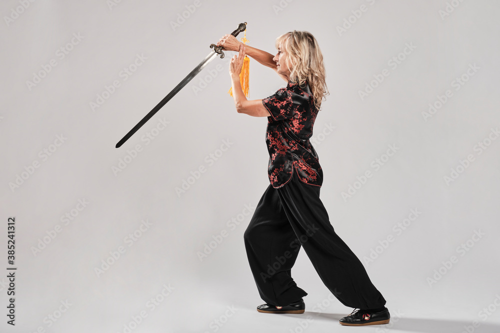 Mature blonde woman practicing Tai Chin with sword in a white ...