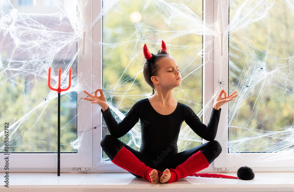 Little girl in costume of little devil doing yoga on window sill Stock ...