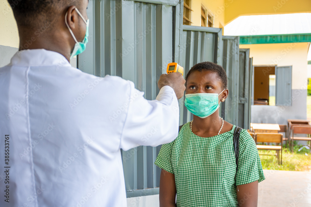 teacher in a school checking kid's body temperature before she enters ...
