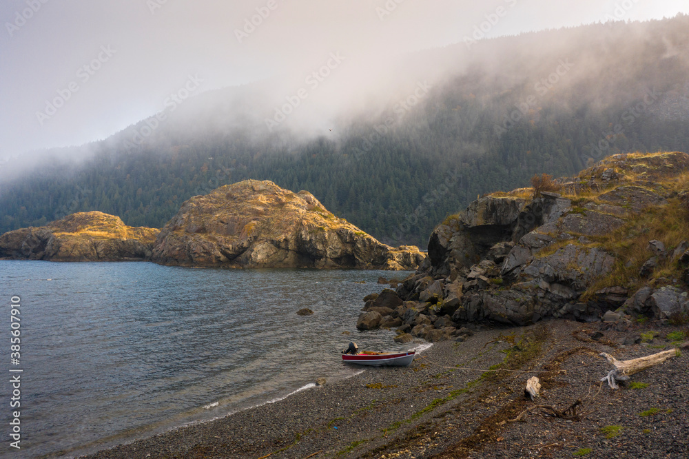 Small Boat On A Rocky Beach With Fog Rolling In. A skiff is pulled on ...
