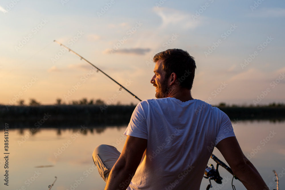 Back view of fisherman sitting at the river dock and fishing at sunset ...