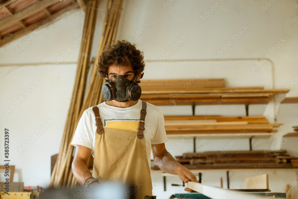 A young man working as carpenter in his wood workshop. Wood worker ...