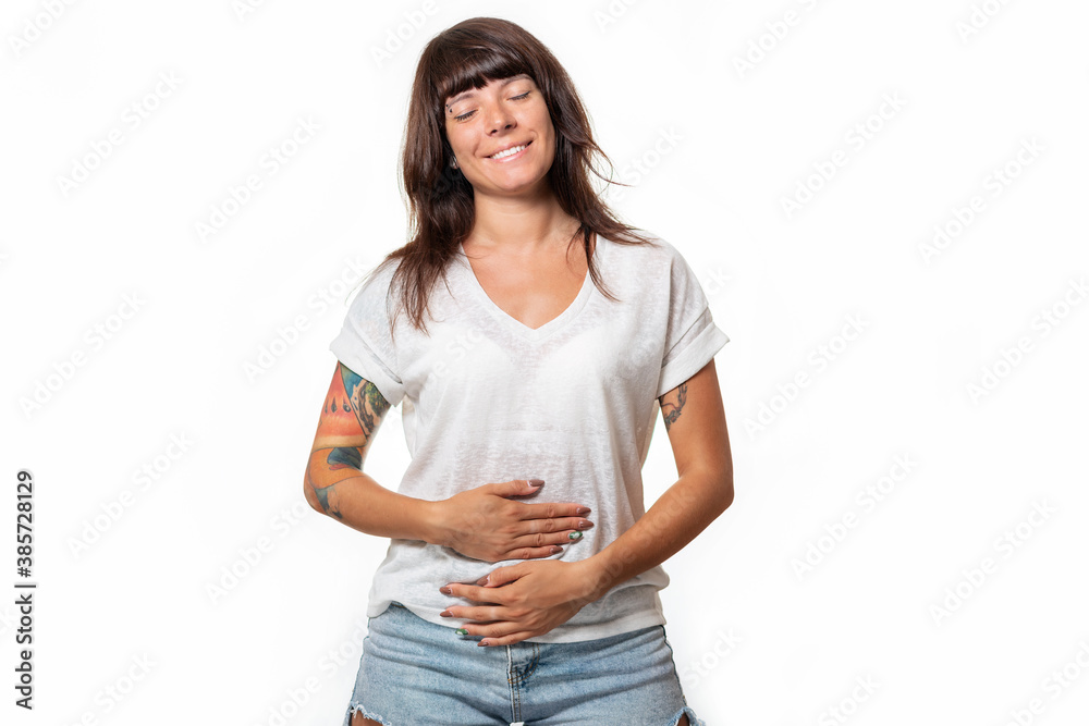 A smiling woman closed her eyes and holds her stomach with hands. White ...
