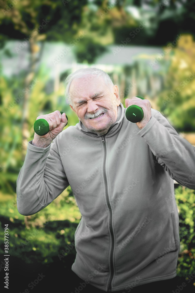 An old man trains his muscles with dumbbells in the Park after a home ...