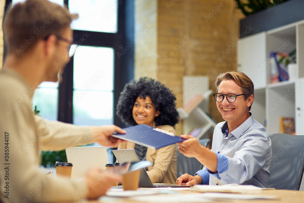 Cheerful man giving a folder with documents to his colleague and ...