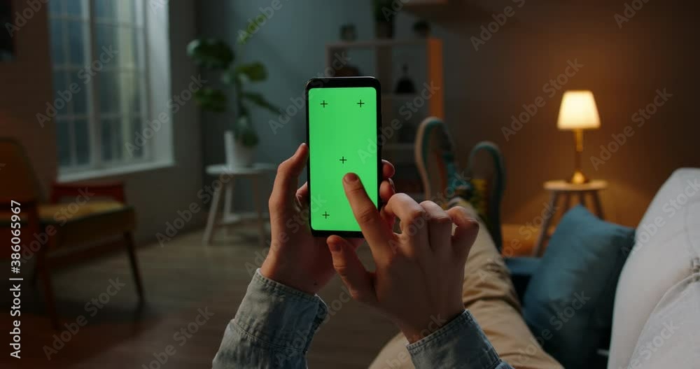 Man lying on couch using smartphone with chroma key green screen at night, scrdoing various ...