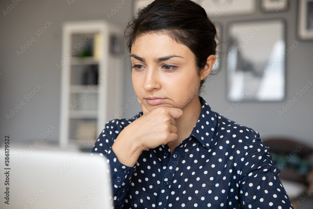 Foto de Unsure Indian business woman sit at desk looks at laptop screen ...