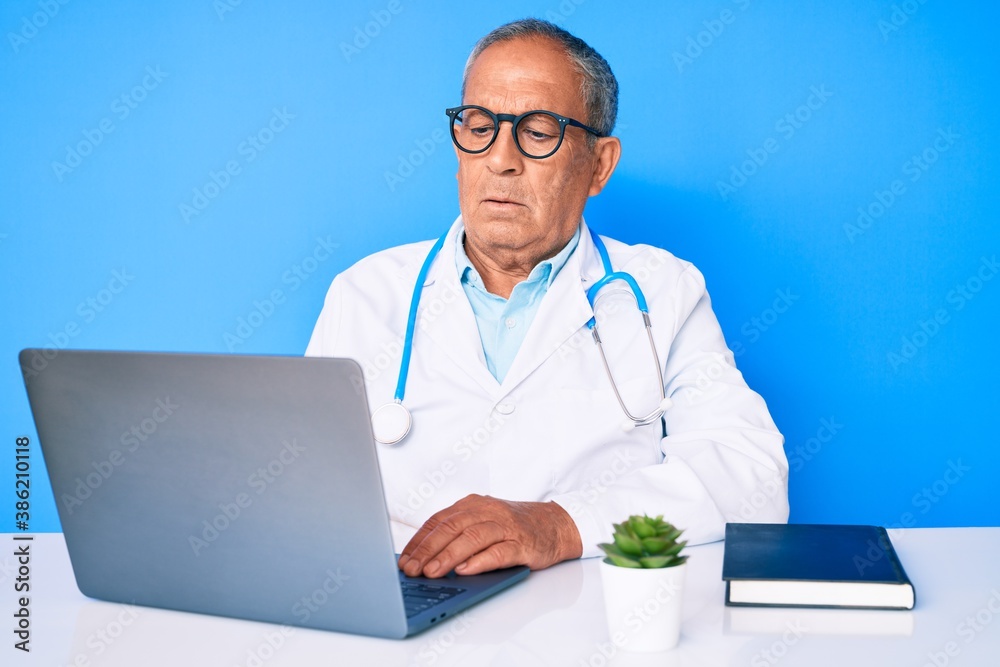 Senior handsome man with gray hair wearing doctor uniform working using ...