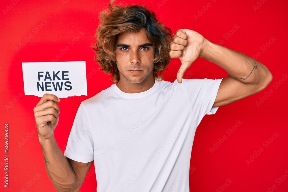 Young hispanic man holding fake news banner with angry face, negative ...