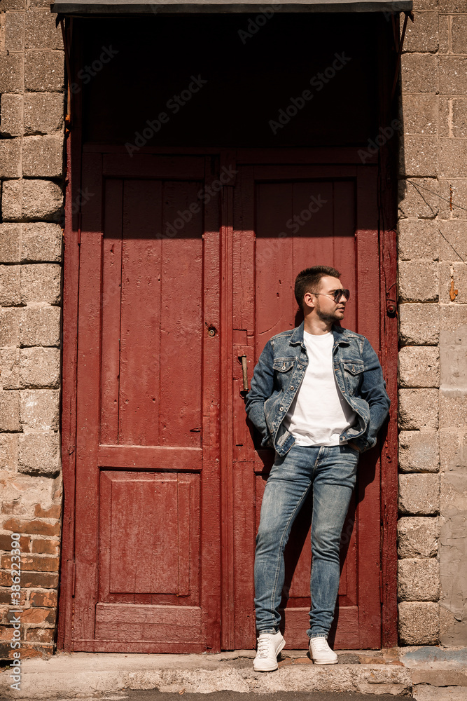 Handsome man with a beard in a denim jacket and denim pants stands near ...