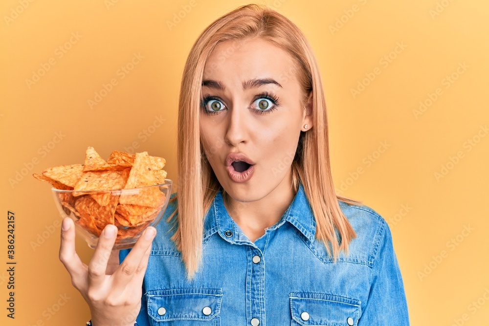 Beautiful caucasian woman holding nachos potato chips scared and amazed ...