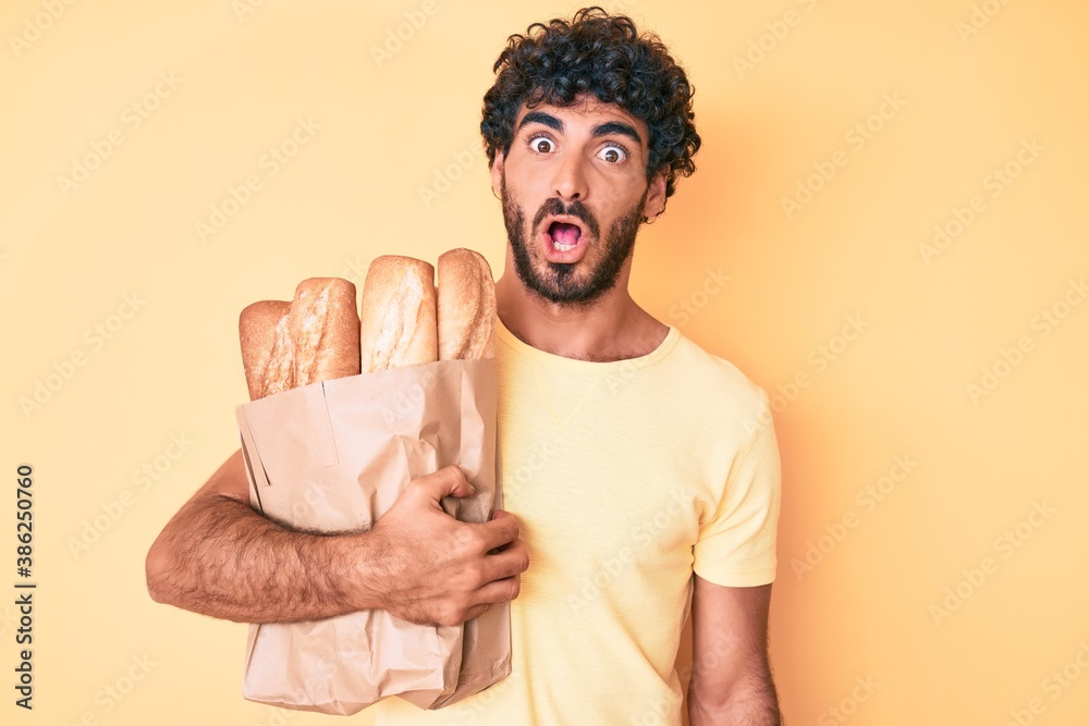 Handsome young man with curly hair and bear holding paper bag with ...