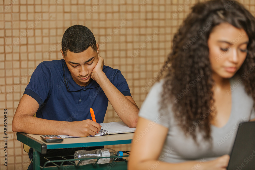 Latin student writing in a notebook with one arm holding his face in ...