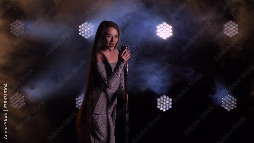 A beautiful young vocalist with long hair gives a concert on stage in ...