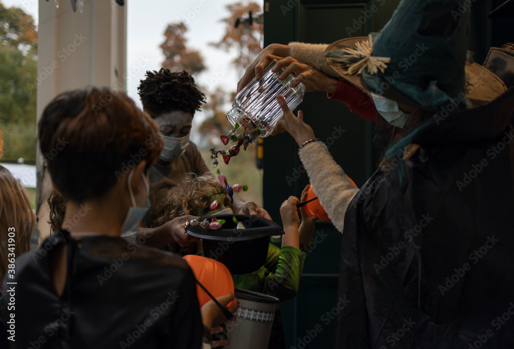 Hosts giving candies to a group of trick-or-treating kids during ...