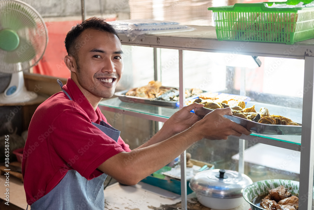 The food stall vendor smiles looking at the camera while holding the ...