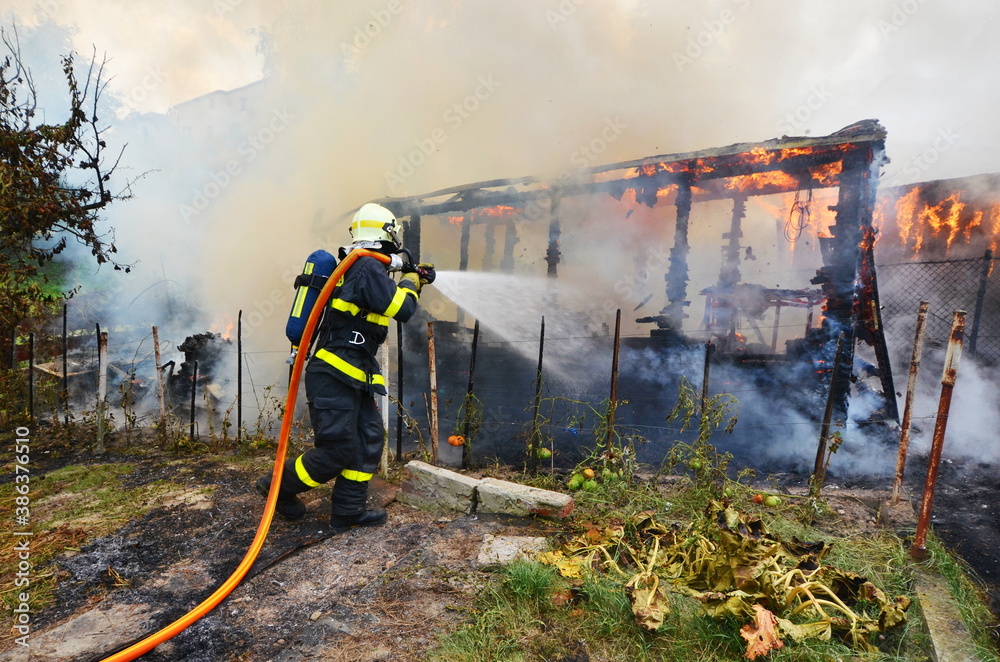 Firefighter uses water from hose to extinguish a huge fire of wooden ...