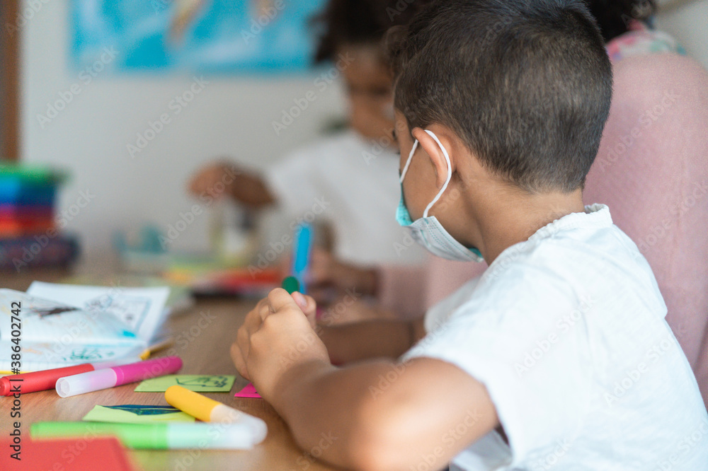Boy painting in preschool classroom wearing face protective mask - Back ...