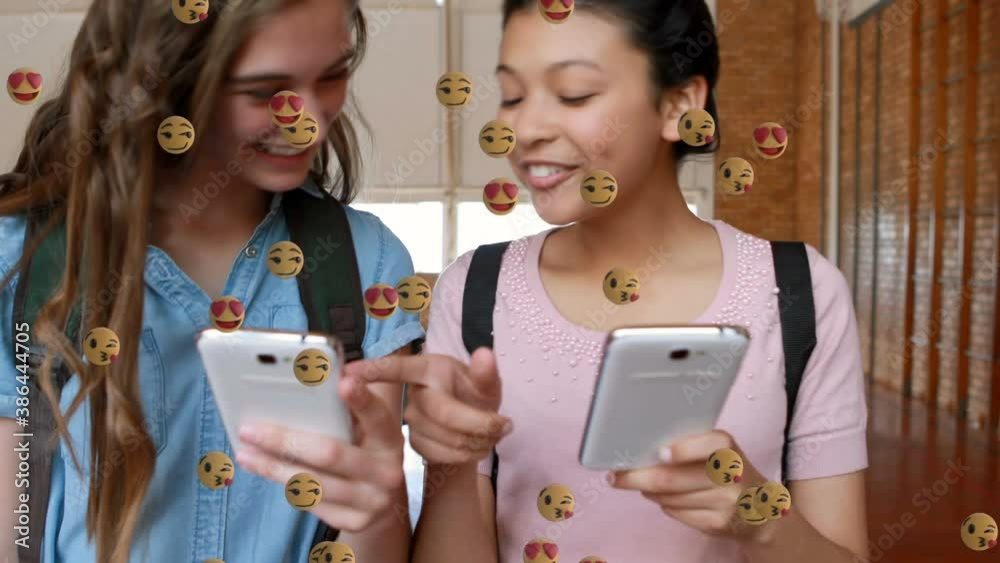 Multiple face emojis floating against two female students using ...