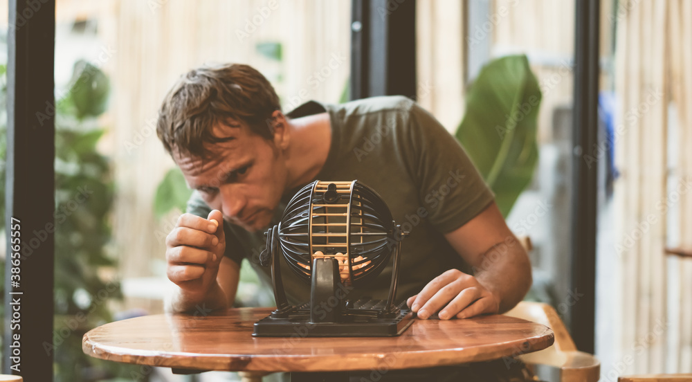 Young man in green shirt hold lotto sphere spins small balls, table ...