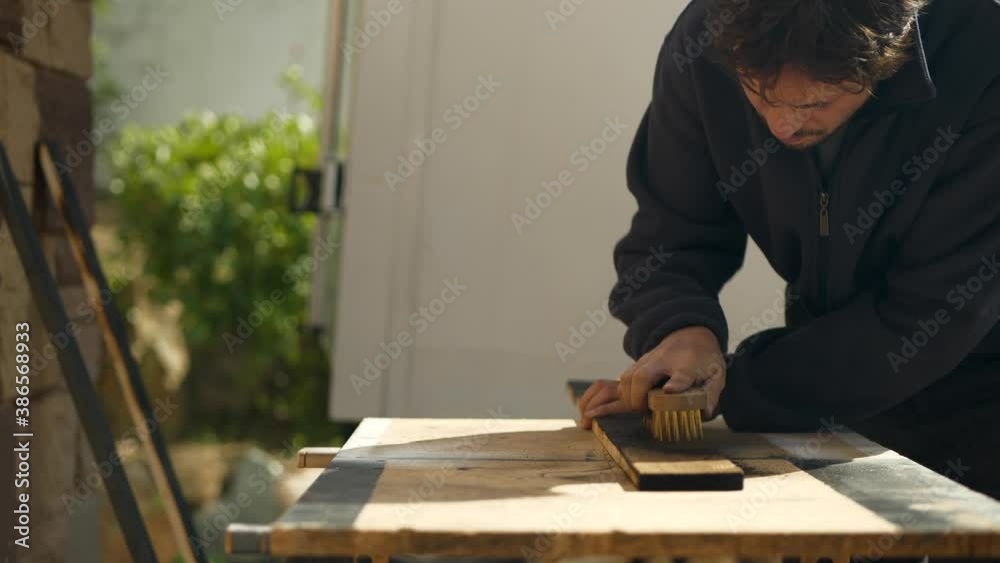 Craftsman scrapes char from torched wood plank with wire brush outside ...