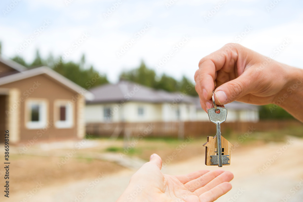 Hand with a key and a wooden key ring-house. Background of fence and ...