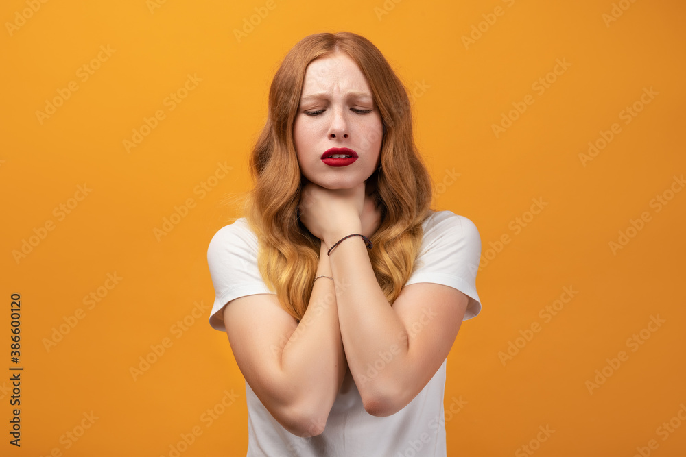 Frustrated girl with wavy redhead, keeps hands on neck, has painful ...
