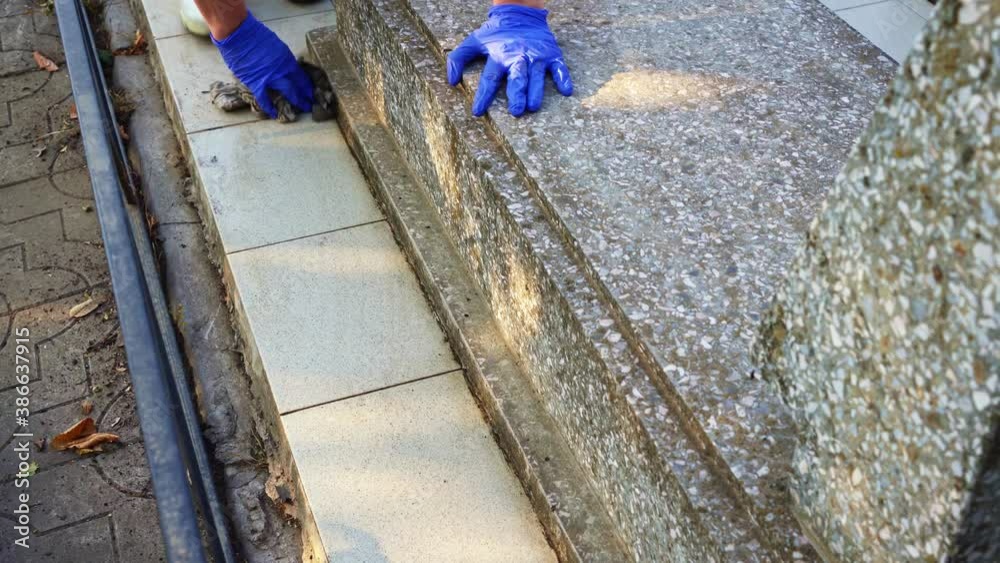 Cleaning cemetery. A woman washes grey paving slabs and monument grave ...