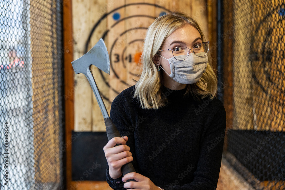 Teenage girl holds axe at an axe throwing range with target behind her ...