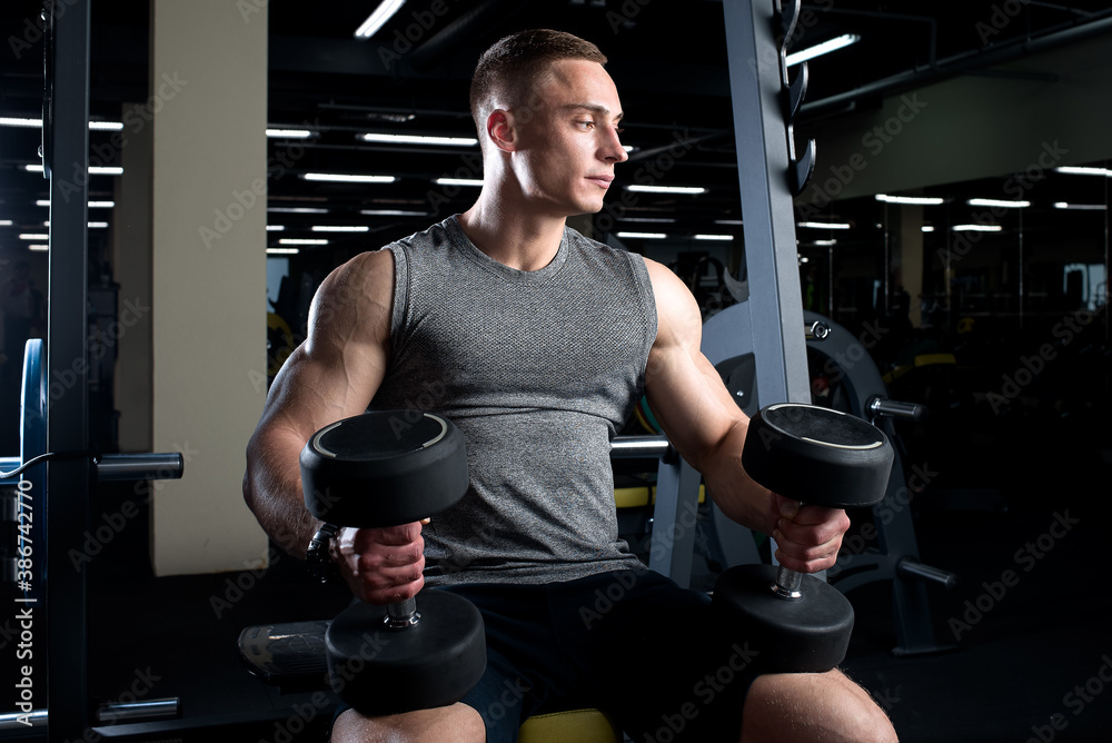 A muscular man is holding dumbbells on his knees in a gym. A ...