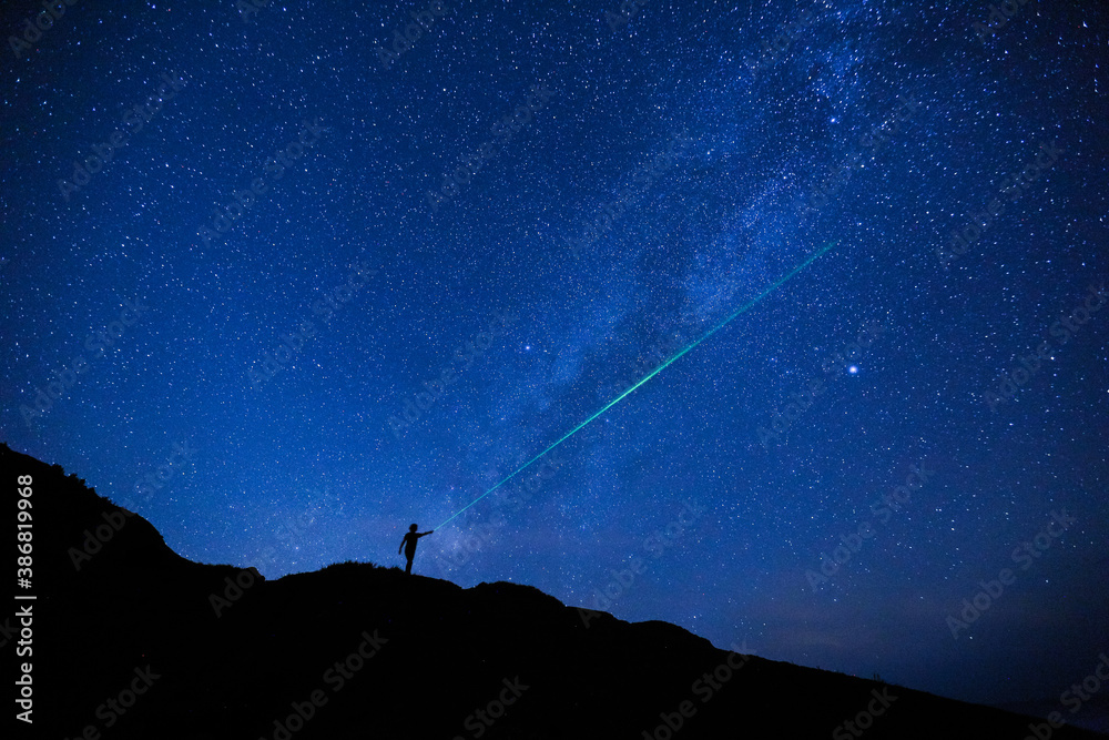 Silhouette of girl / woman standing on the hill use a laser pointer to ...