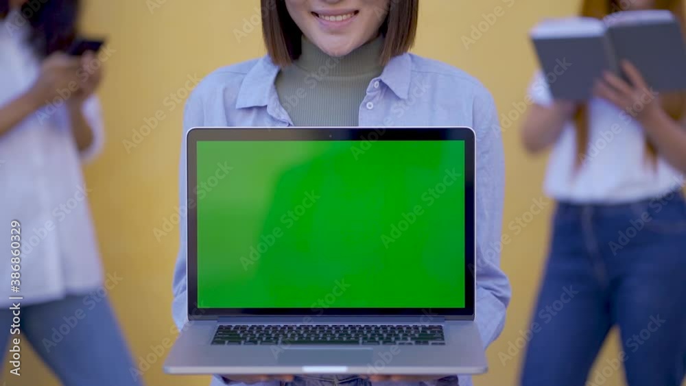 Woman holding a laptop with green screen. Chroma key. People behind ...