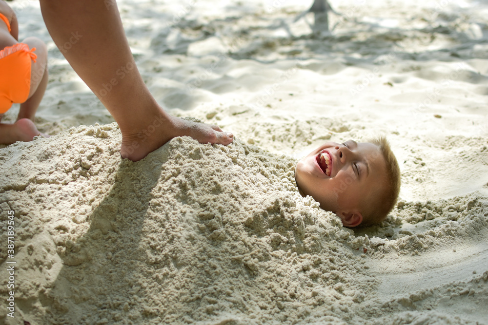 child boy playing in the sand on the beach, child burrowing under the ...