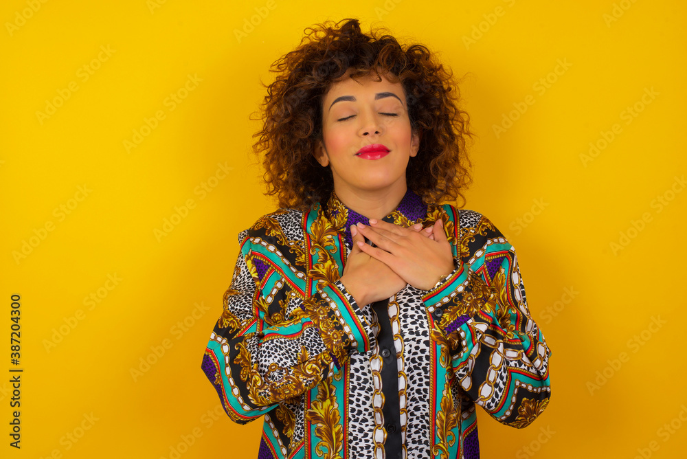 Faithful woman closes eyes and keeps hands on chest near heart, shows ...