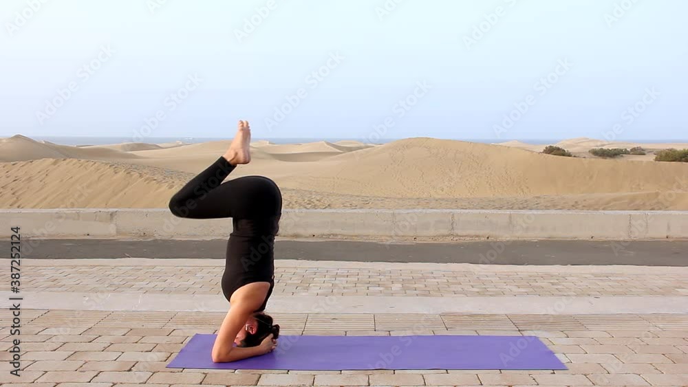 Female yogi doing sirsasana posture sideways at Maspalomas sand dunes ...