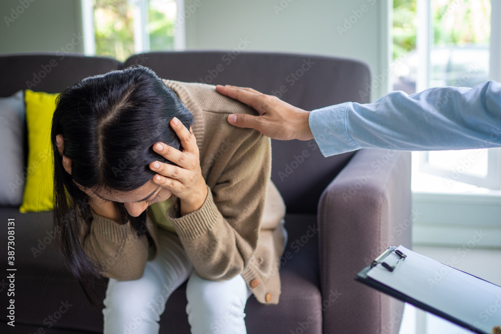 A psychiatrist stands hand on the shoulder of a woman to provide ...