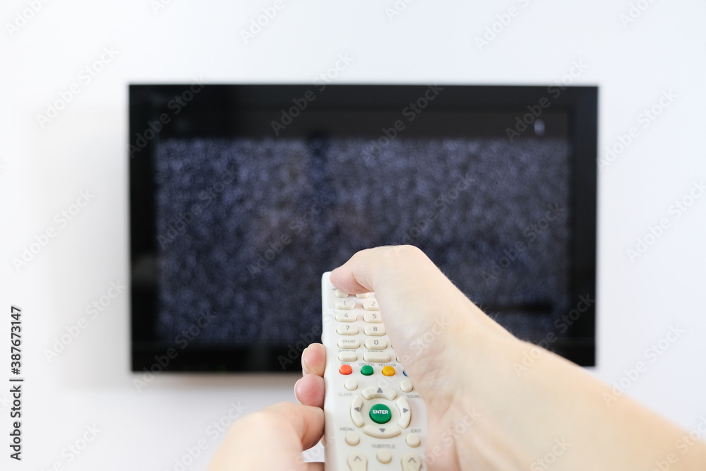 Hand with TV remote control in front of the screen with white noise on ...