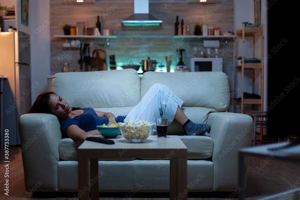 Young woman watching TV and feeling bored sitting on the couch in the ...