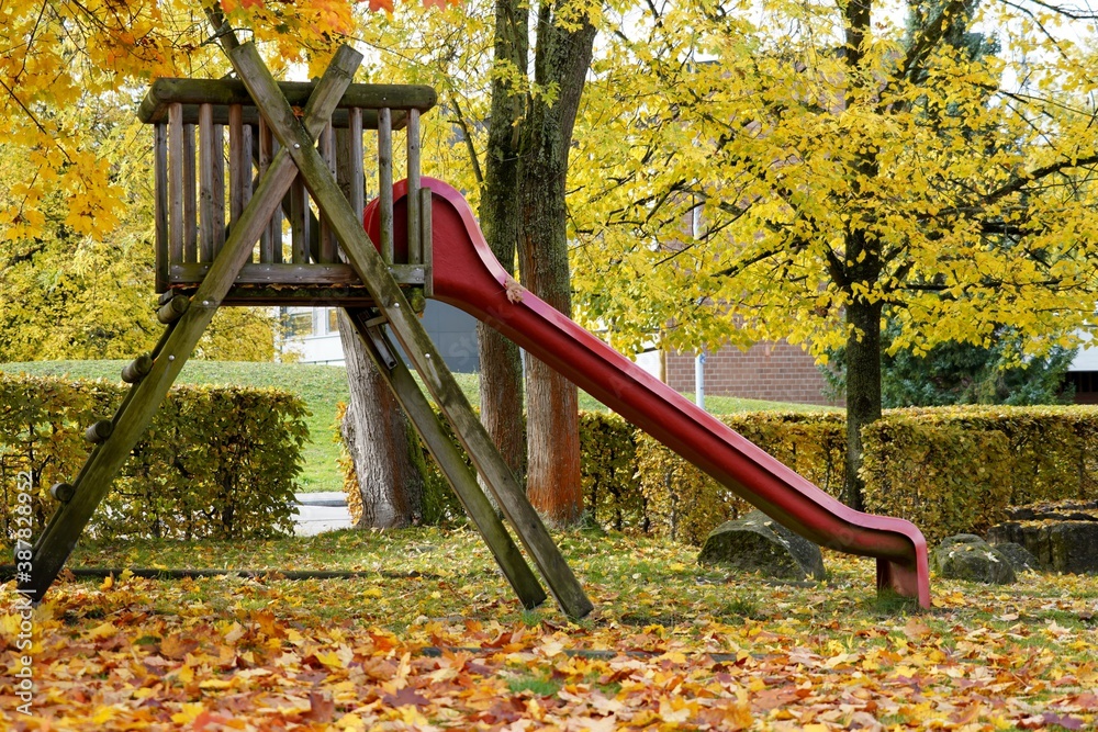 A red slide in the park in autumn in lateral view surrounded by foliage ...