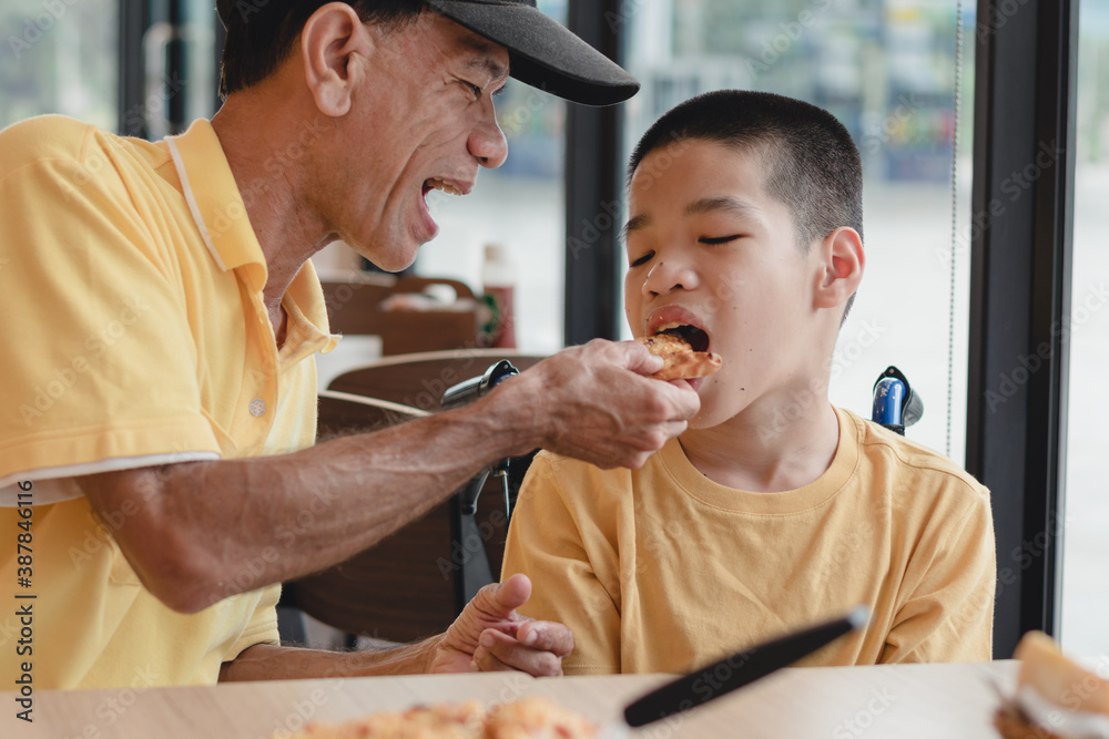 Father feeding food to Disabled child on the wheelchair in pizza shop ...