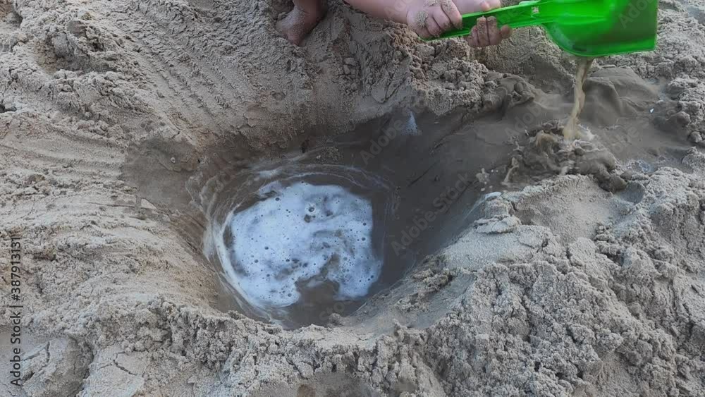 A child digging a pit on the beach. A girl playing with mud on the ...