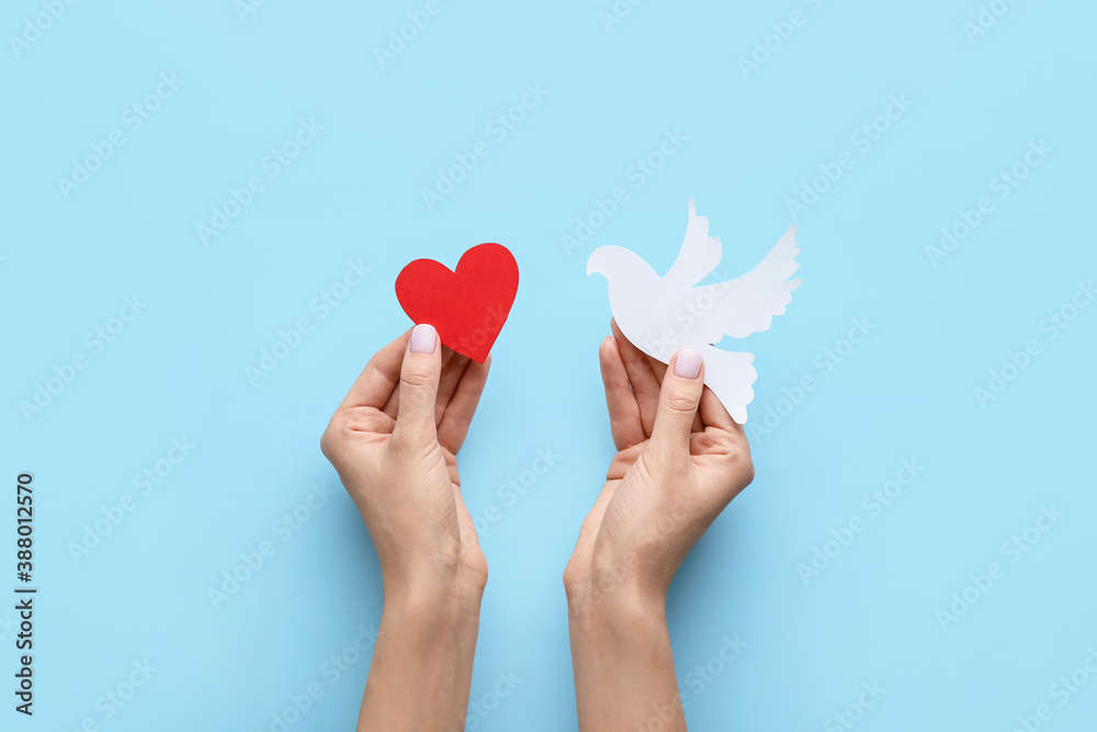 Female hands with paper dove and heart on color background ...