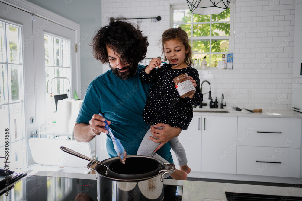 father holding daughter while cooking on stove top in modern kitchen ...