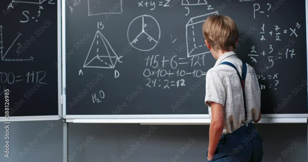 Rear on Caucasian small teen boy standing at blackboard in classroom ...