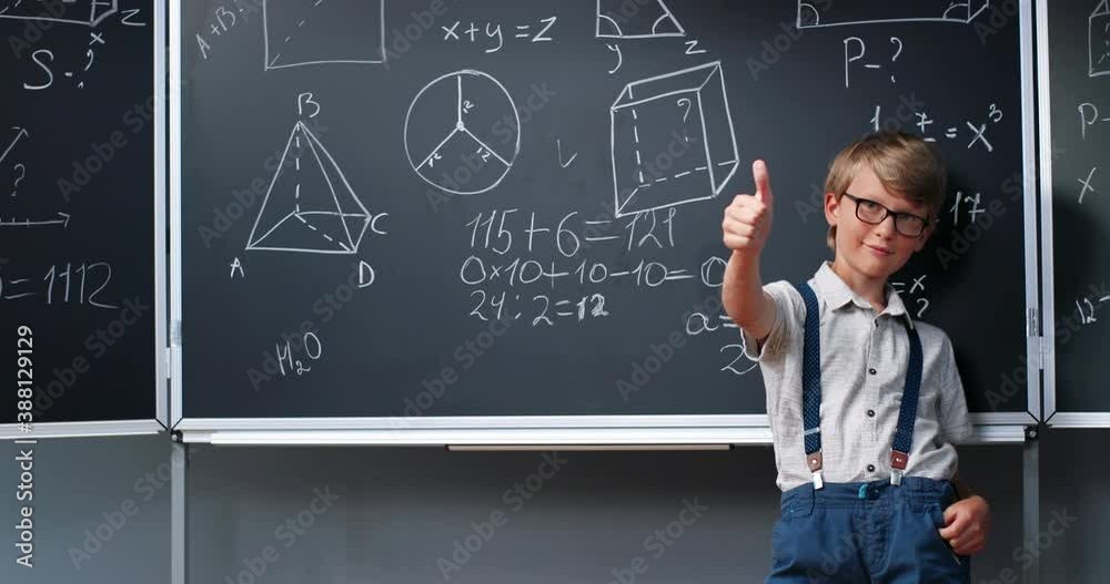 Caucasian small boy in glasses thinking at blackboard in classroom ...