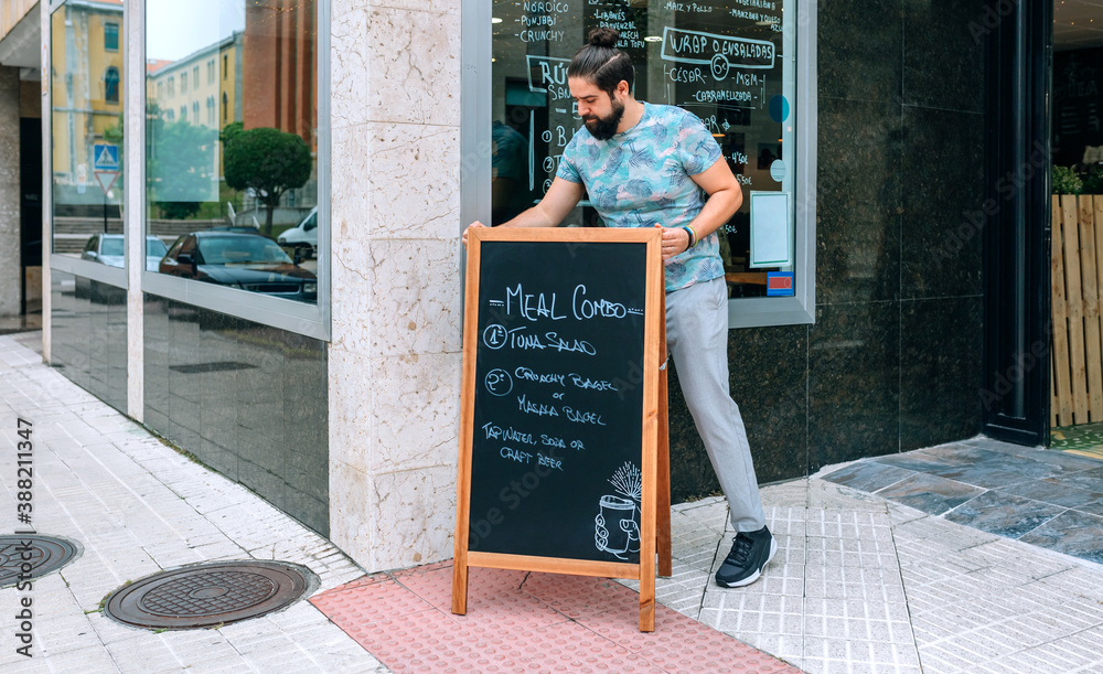Young waiter placing a blackboard with the daily menu in front of the ...